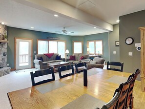 Uma sala de estar espaçosa com uma grande mesa de jantar de madeira, várias cadeiras, um sofá e um ventilador de teto.