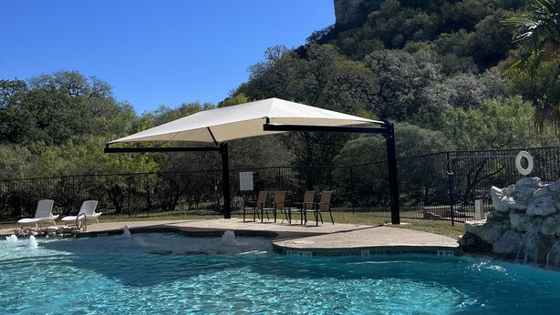 Piscina azul límpida com borda de pedra, rodeada por espreguiçadeiras e área com sombra.