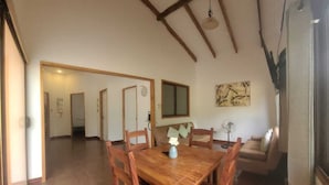 Uma sala de jantar ampla com uma mesa e cadeiras de madeira, um ventilador e um sofá ao fundo.
