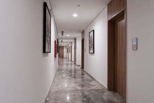 Corredor moderno de hotel, com piso de mármore polido, obras de arte emolduradas nas paredes e um painel de elevador digital.