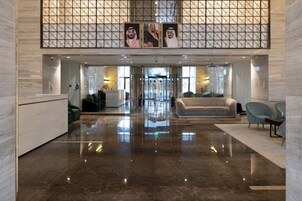 Um hall amplo com piso de mármore polido, balcão de recepção, área de estar e um elevador de vidro.