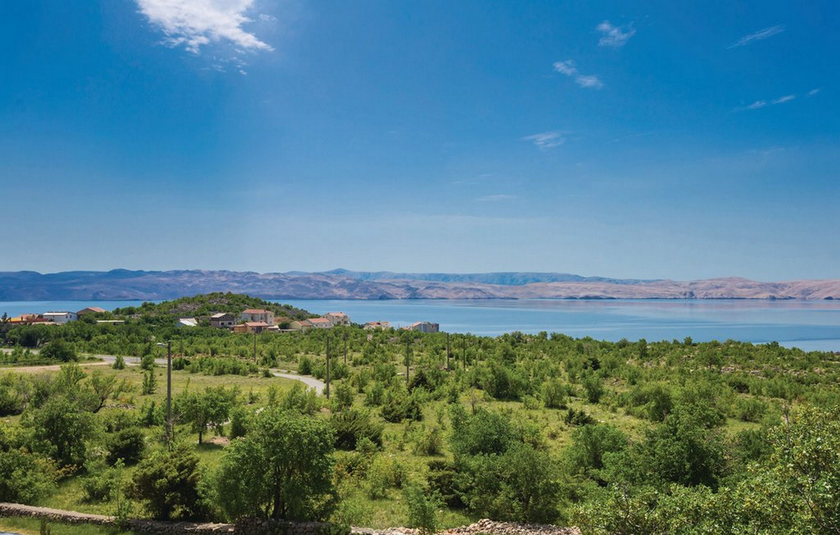 Paisagem costeira com vista clara para o mar, um pequeno povoado com casas e um relevo montanhoso ao fundo.