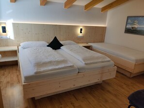 Uma cama com estrutura de madeira, dois travesseiros, uma mesa de cabeceira, uma luminária na parede e um quadro.
