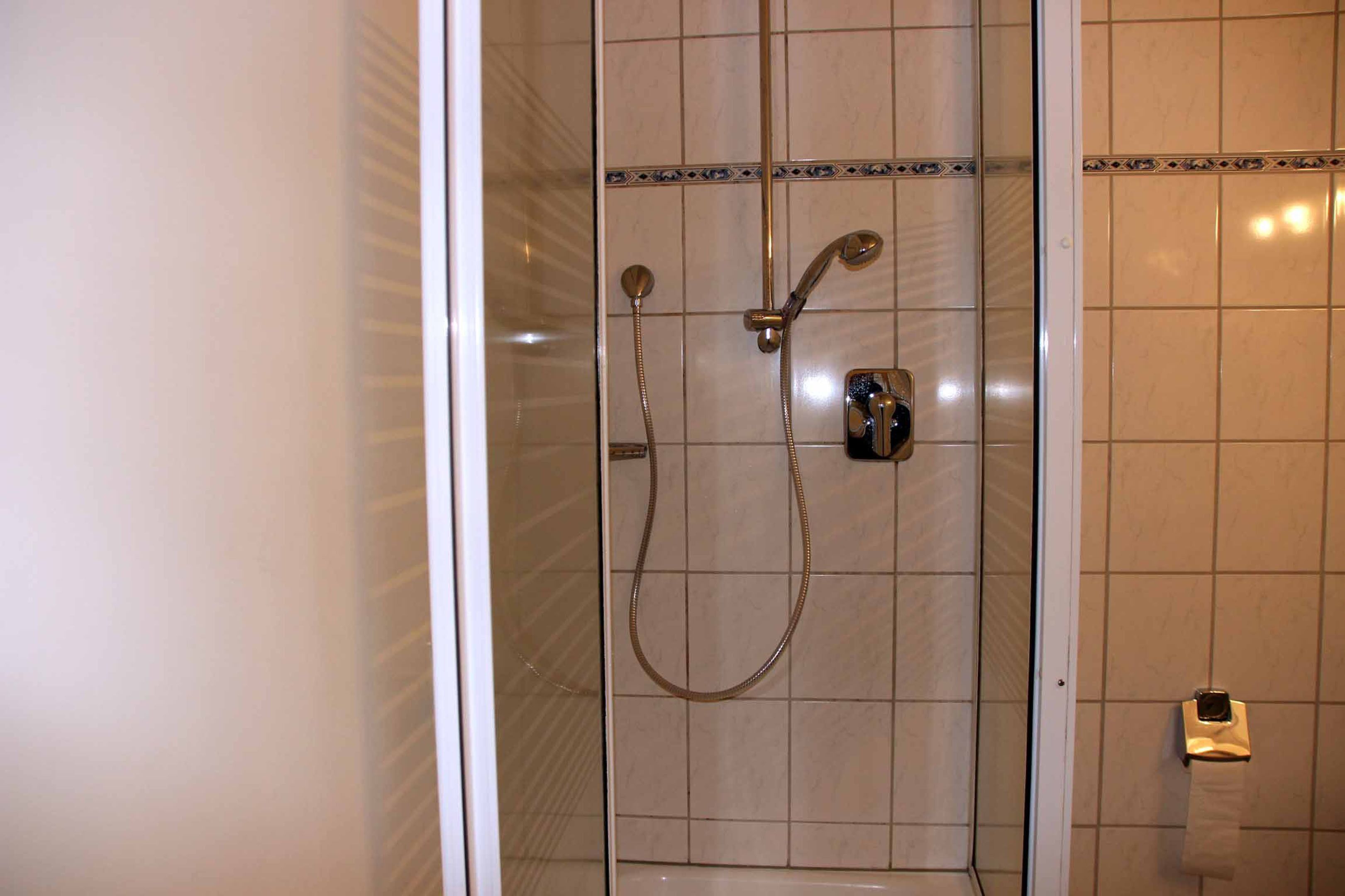 Um chuveiro com box de vidro, um chuveiro manual e uma torneira fixada na parede.