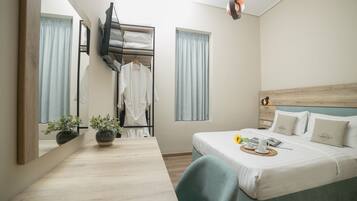 Quarto de hotel com cama, escrivaninha, espelho, televisão e duas janelas com cortinas.