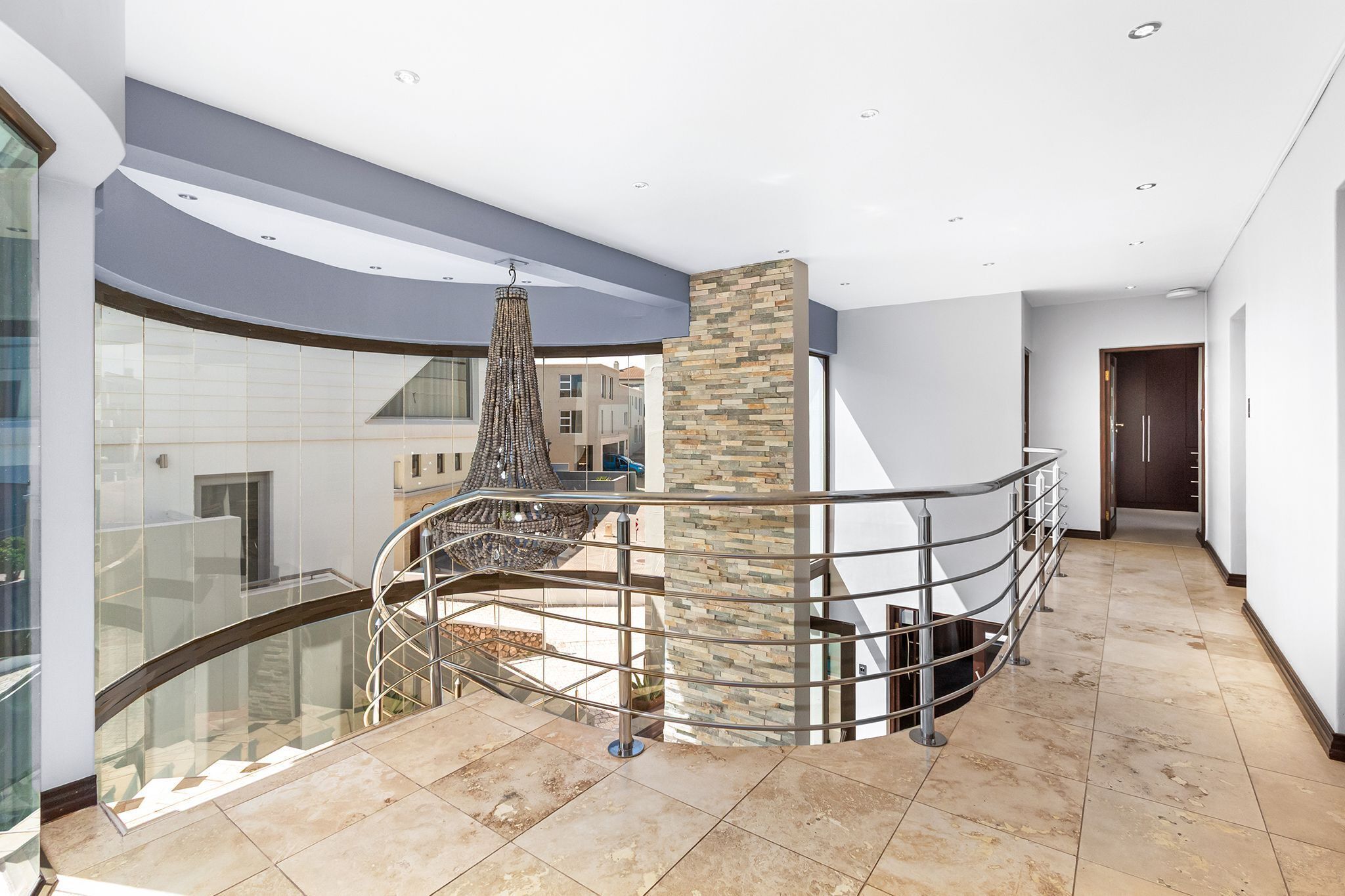 Um interior espaçoso com guarda-corpo de vidro curvo, parede de destaque em pedra e vista para a cidade.
