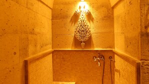 Um banheiro com piso em azulejos, pia, chuveiro e um lustre decorativo.