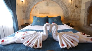 Cama com colcha azul, duas almofadas e dois toalhas em formato de cisne com pétalas de rosa.