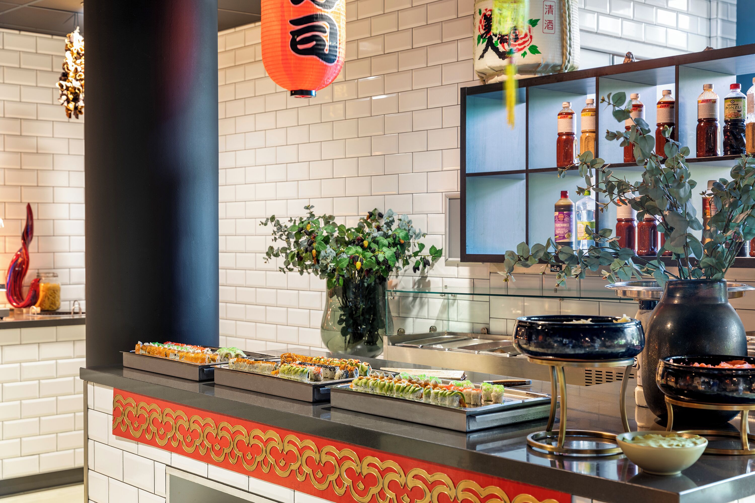 Uma área de buffet com sushi, um vaso de flores e frascos de condimentos.