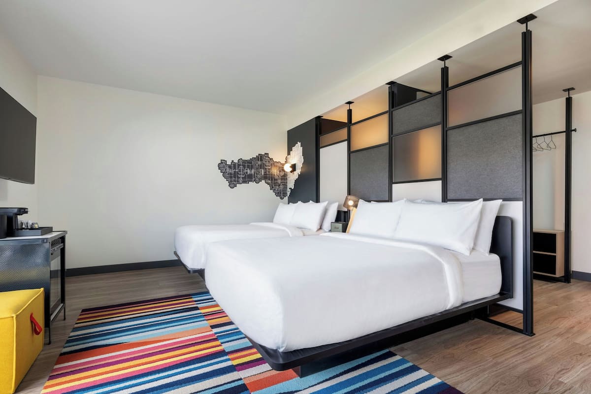 Quarto de hotel moderno com uma cama grande, uma escrivaninha e um tapete listrado e colorido.