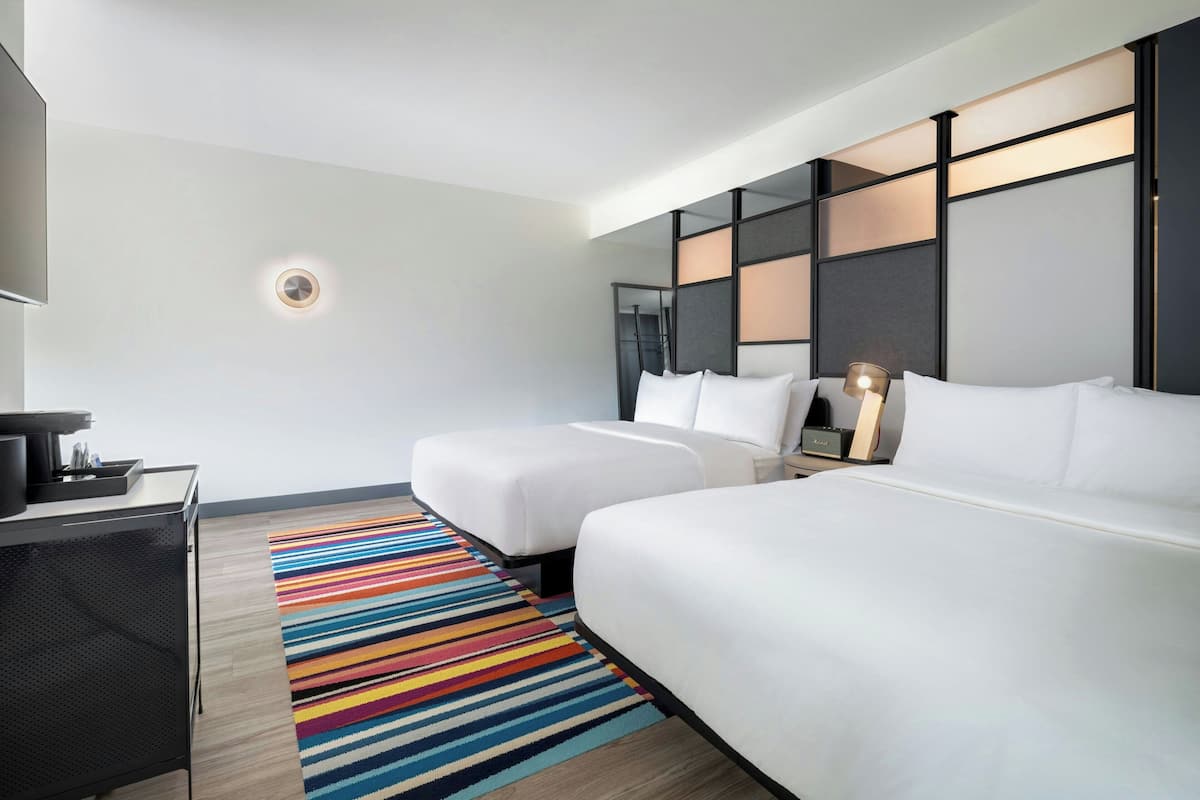 Quarto de hotel com duas camas, uma escrivaninha, um tapete listrado e um design moderno na parede.