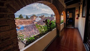 Um corredor com um arco de tijolos que dá para um terraço com telhado de azulejos e plantas.