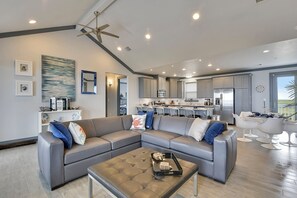 Uma sala de estar moderna com um sofá seccional, uma mesa de centro e um espaço de jantar com cadeiras brancas.