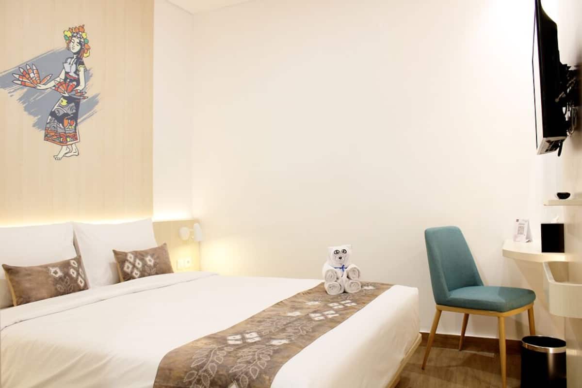 Quarto de hotel com cama, cadeira, televisão e uma pequena mesa.