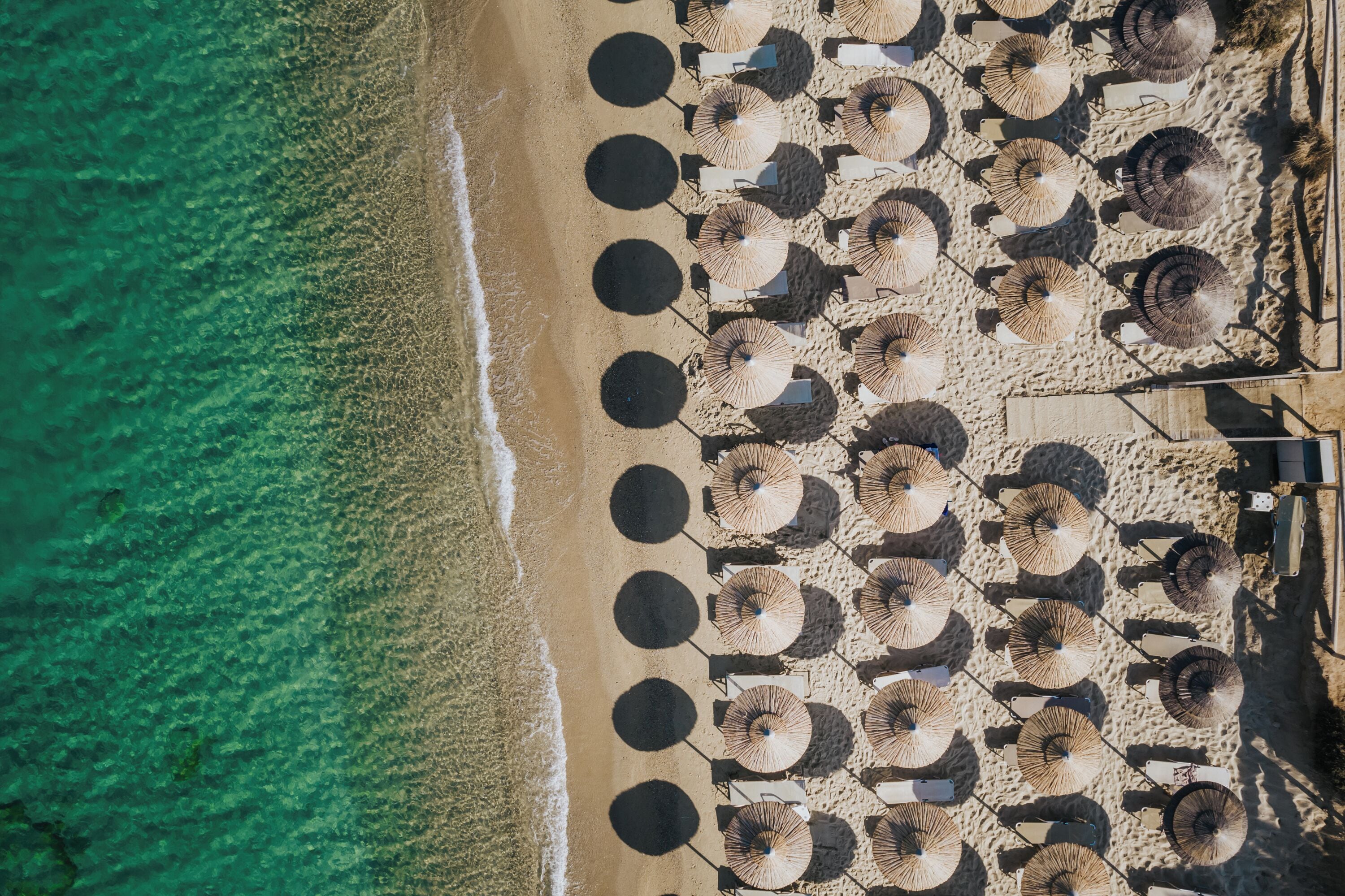 Vista aérea de uma praia com fileiras de guarda-sóis e cadeirões de praia.