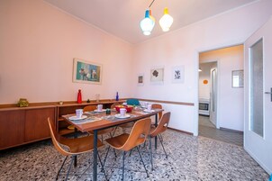 Uma área de refeições com uma mesa posta para quatro pessoas, cadeiras, um armário de madeira e um quadro na parede.
