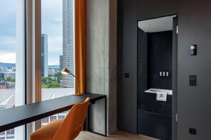 Quarto moderno com escrivaninha, cadeira e vista para edifícios altos.