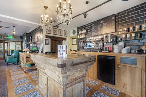 Uma área de bar com balcão de madeira, um candelabro e um quadro de cardápio.