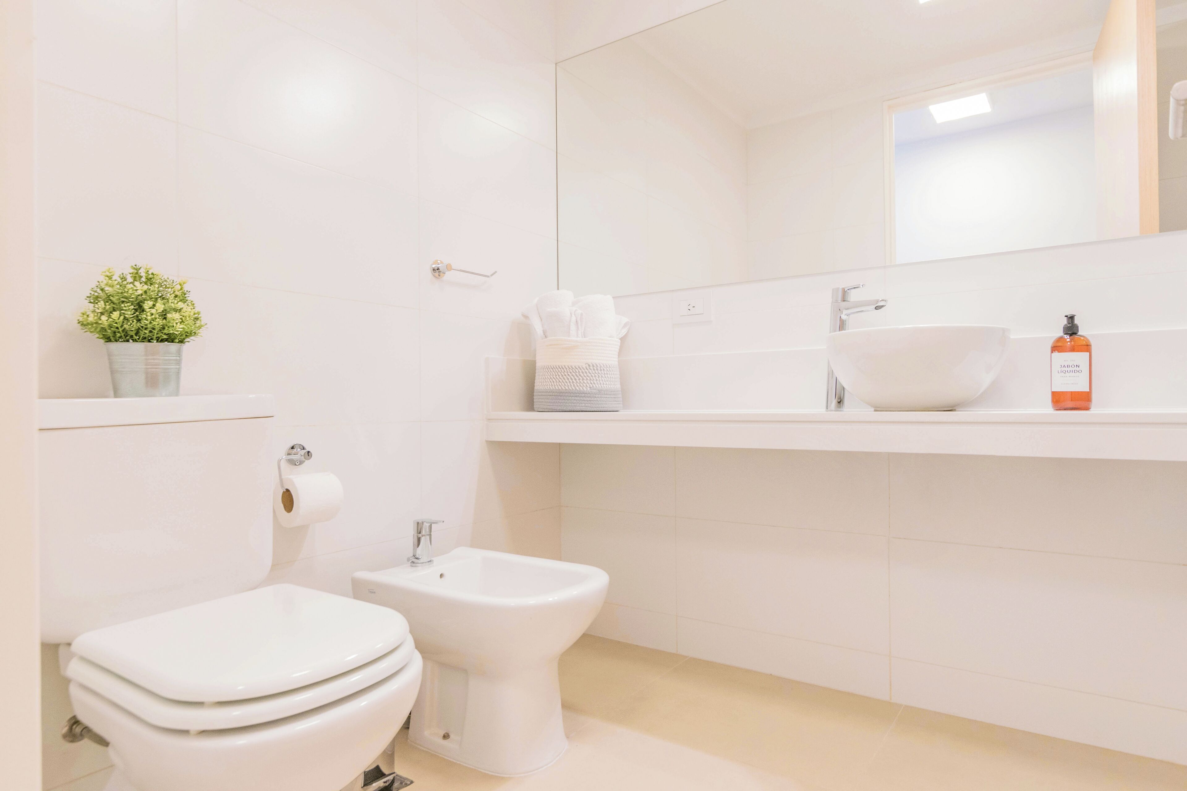 Uma casa de banho moderna com sanita, bidé, lavatório branco e uma pequena planta num vaso.