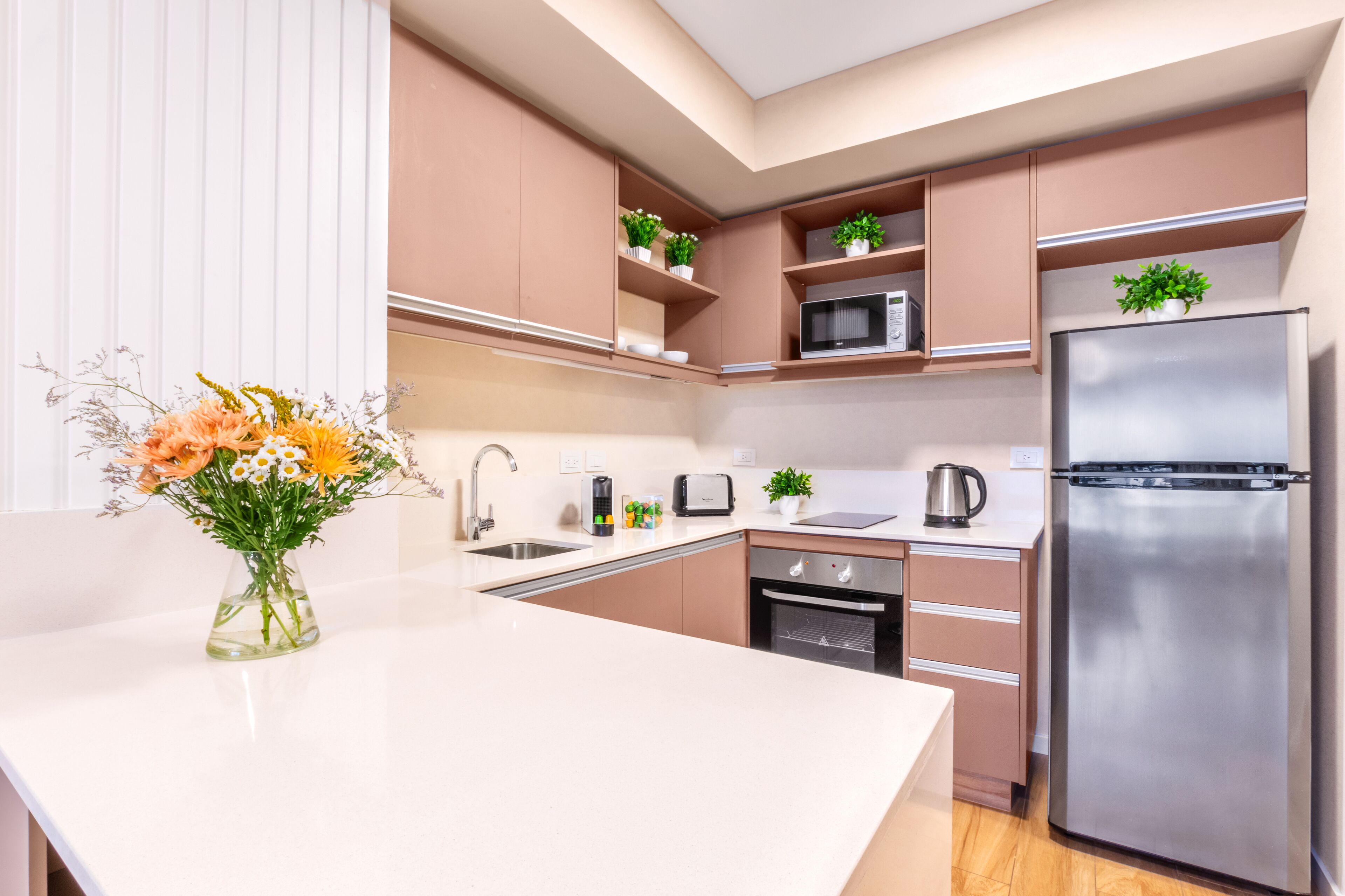 Uma cozinha moderna com ilha central, eletrodomésticos de aço inoxidável e prateleiras embutidas com plantas em vasos.