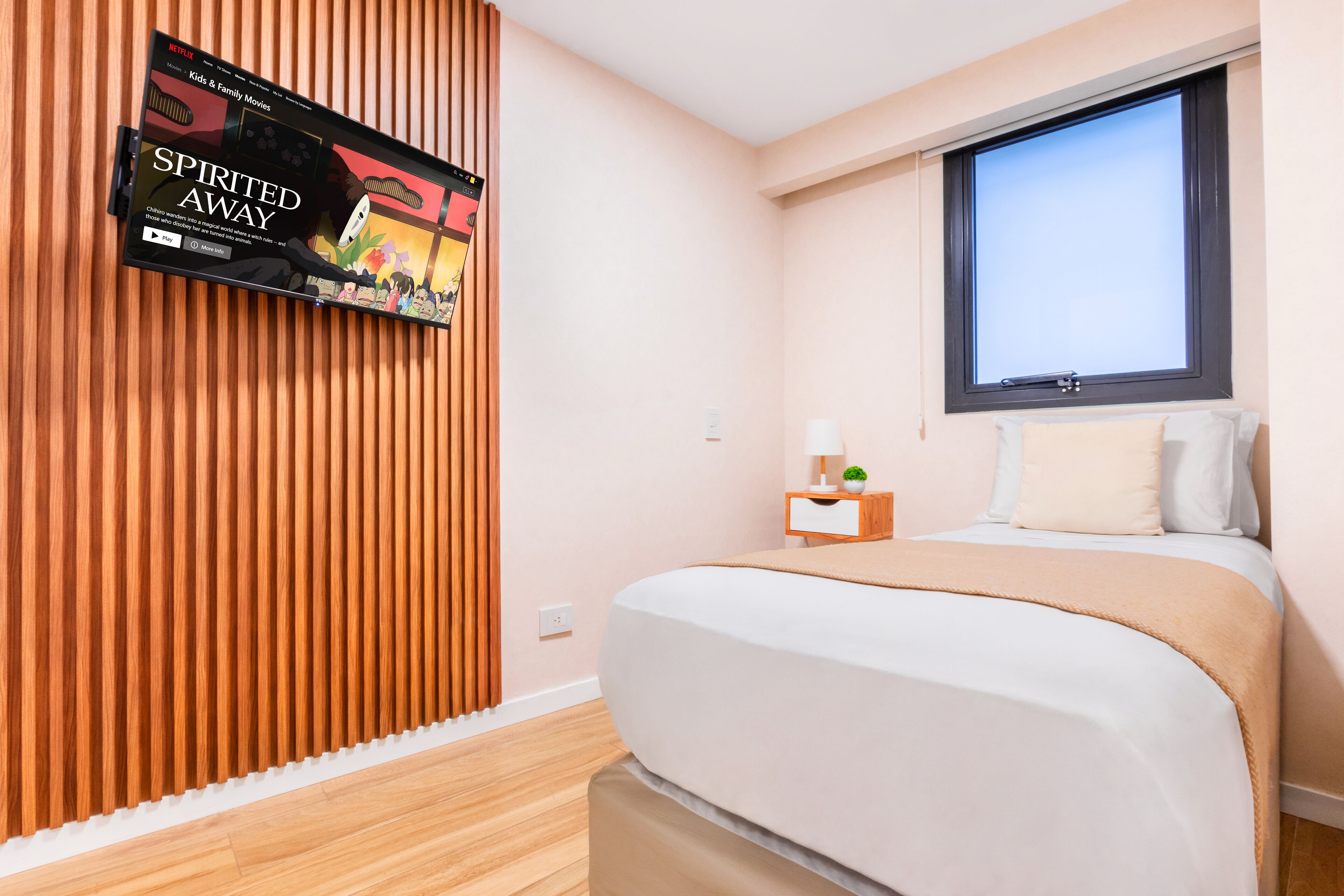 Quarto de hotel com cama, televisão fixada em uma parede revestida de madeira, janela com vista e mesa de cabeceira com abajur.