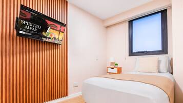 Quarto de hotel com cama, televisão fixada em uma parede revestida de madeira, janela com vista e mesa de cabeceira com abajur.