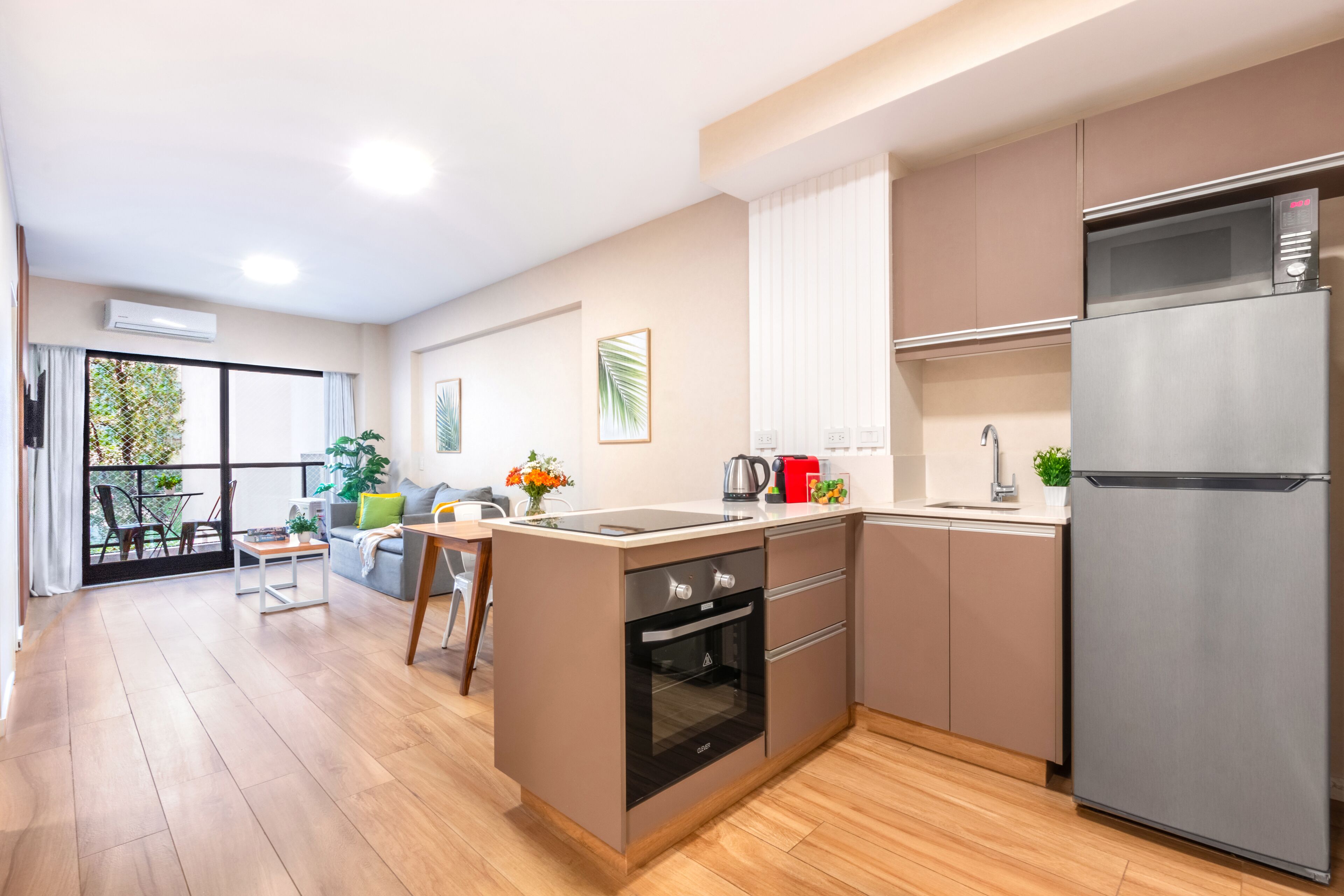 Cozinha moderna com forno embutido, geladeira de aço inoxidável e área de refeições com mesa e cadeiras.