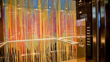 Um elevador com parede de listras verticais coloridas e painel de vidro.