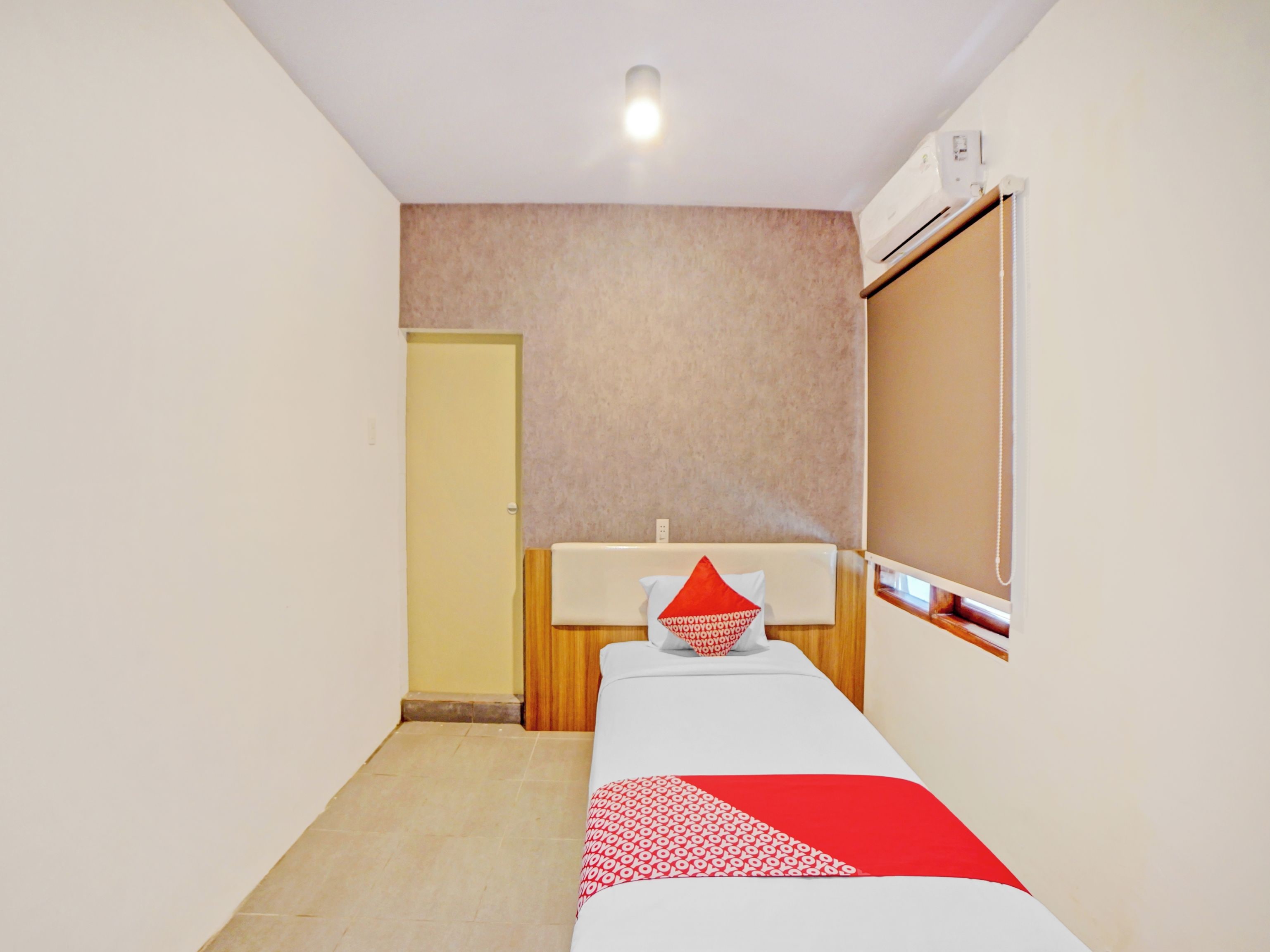Quarto de hotel com uma cama de solteiro, mesa de cabeceira, espelho e janela.