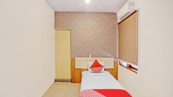 Quarto de hotel com uma cama de solteiro, mesa de cabeceira, espelho e janela.