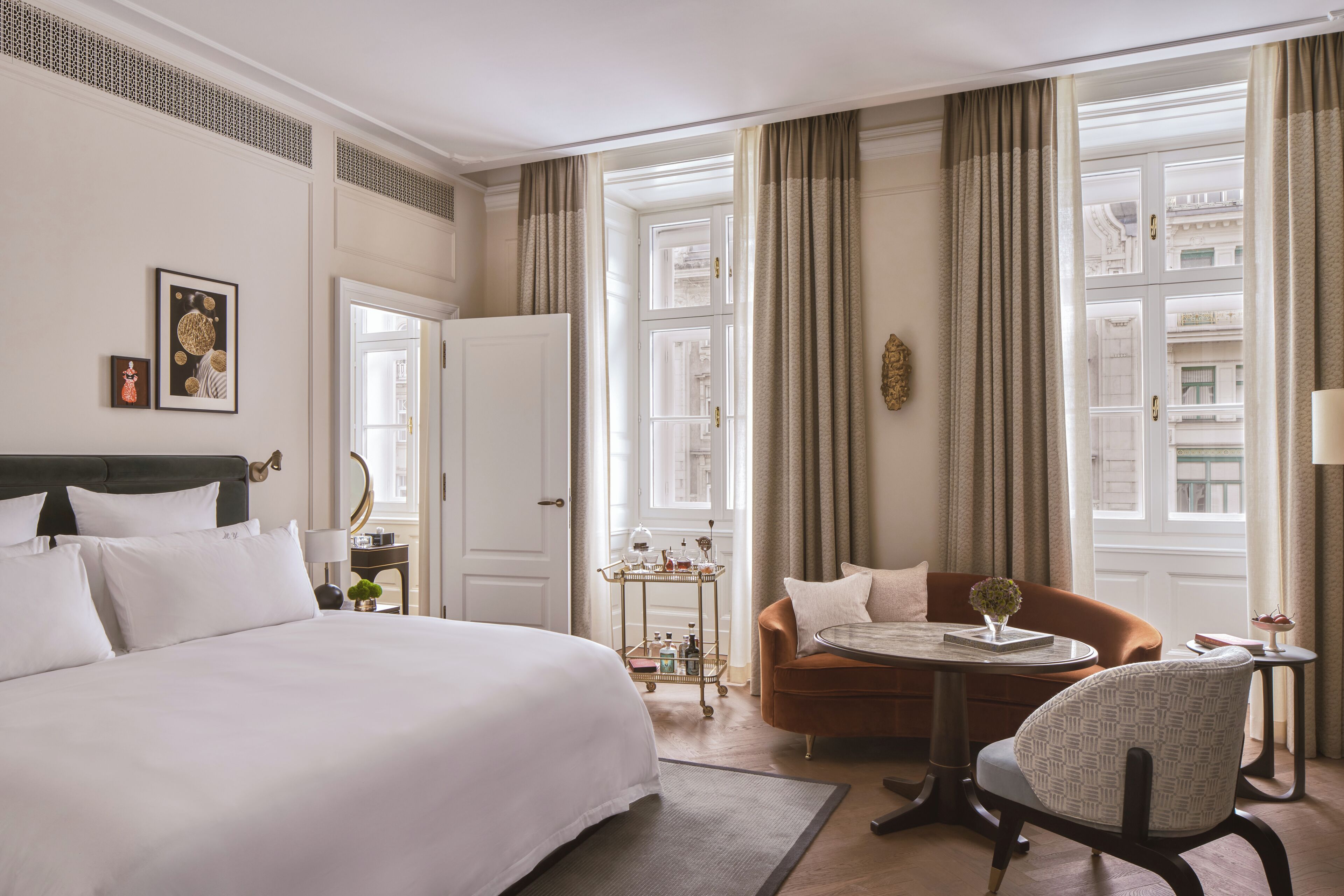 Quarto de hotel com cama, área de estar com mesa e janelas amplas com cortinas.