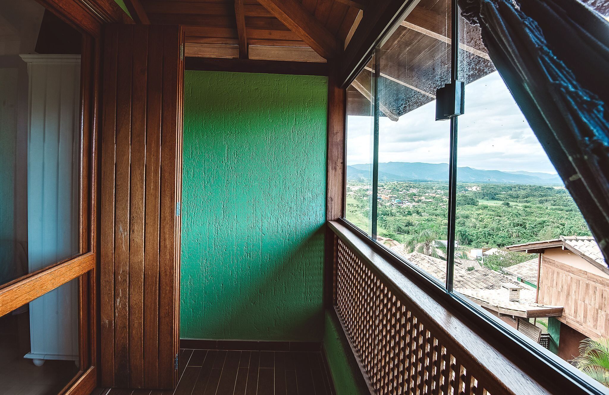 Quarto com parede verde, piso de madeira e janela com vista para uma paisagem.