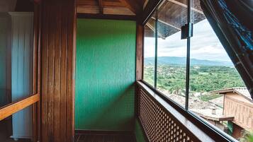 Quarto com parede verde, piso de madeira e janela com vista para uma paisagem.