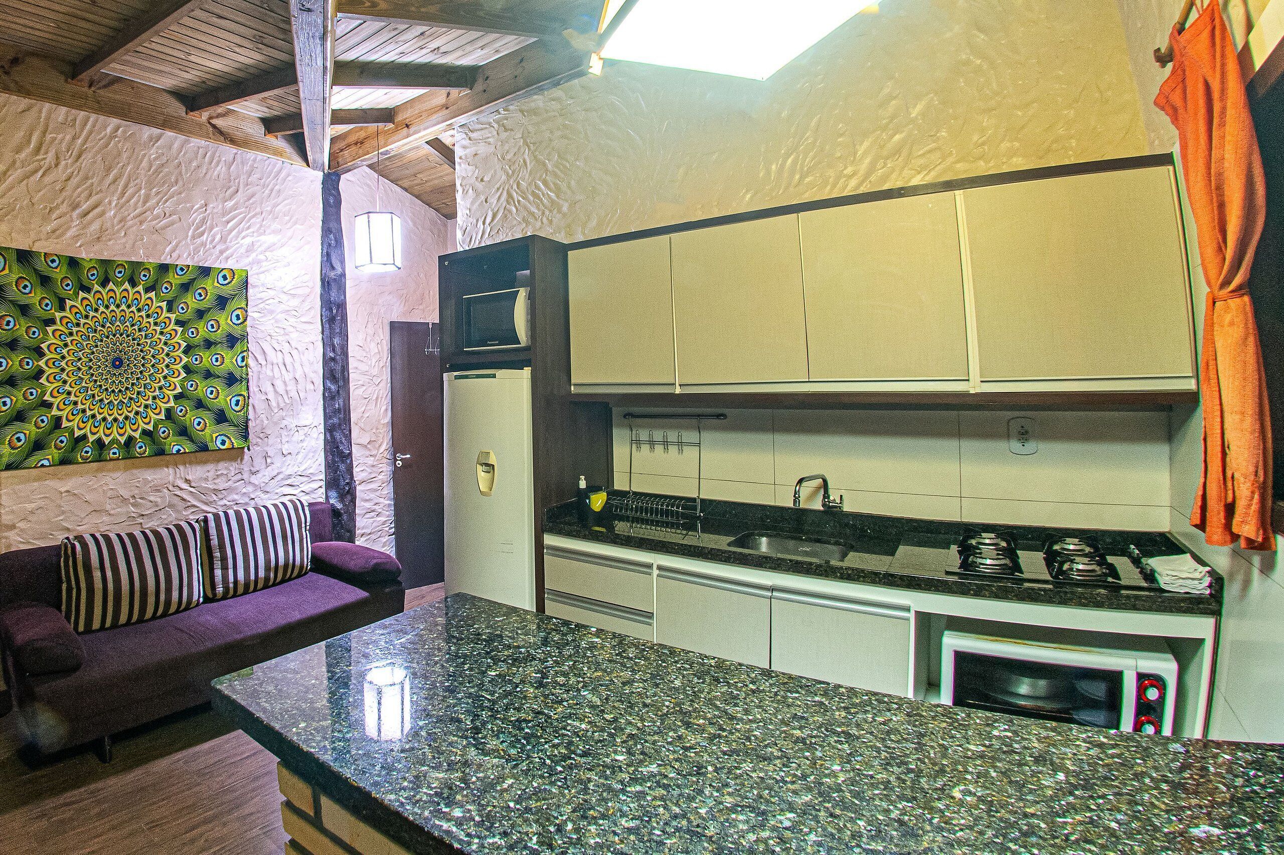 Cozinha compacta com micro-ondas, fogão e pia. Há um sofá com almofadas listradas e um objeto decorativo na parede.