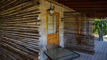 Um deck de madeira com uma mesa de vidro e uma cadeira de vime, uma porta de madeira e cortinas de bambu.