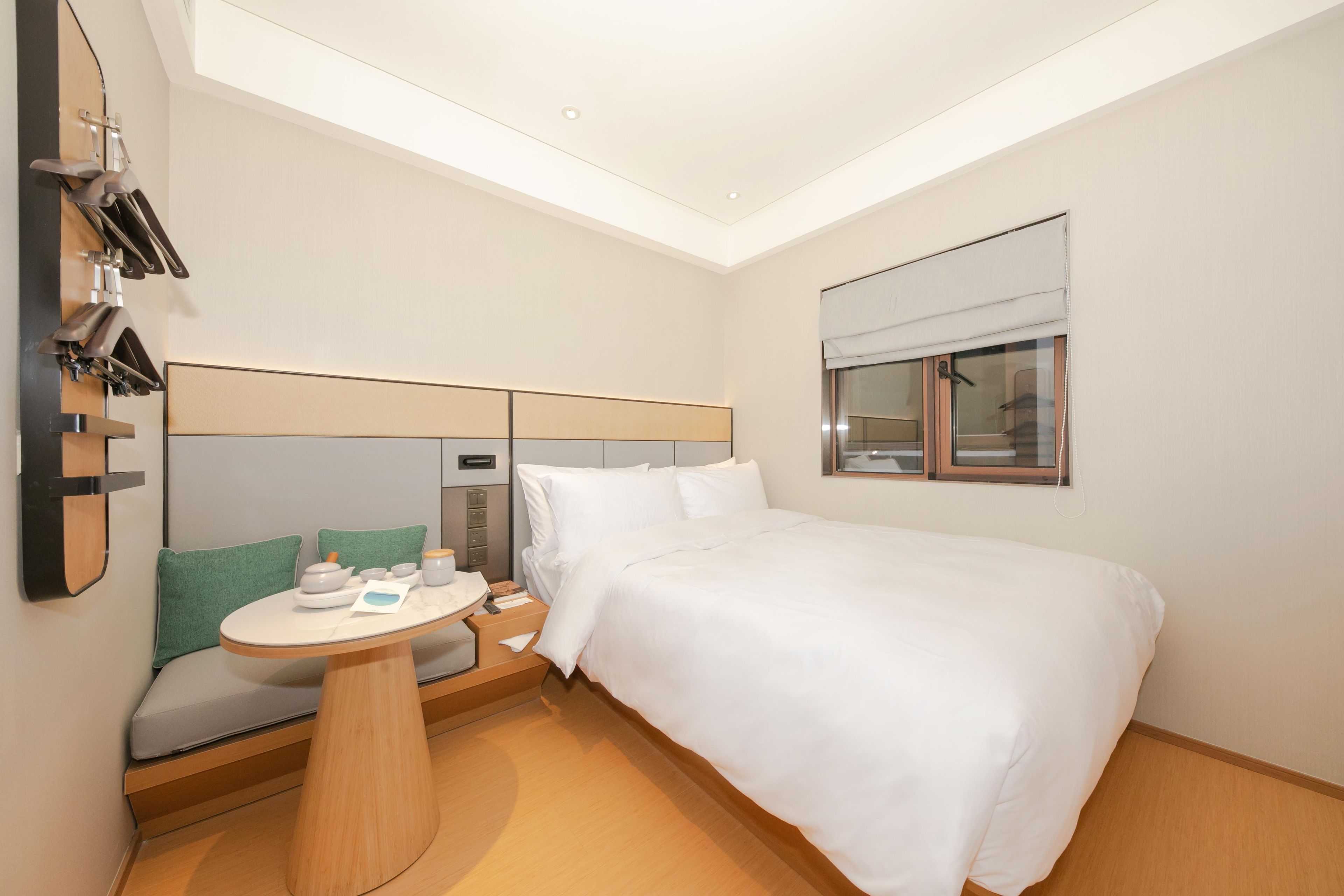 Quarto de hotel com cama, uma mesinha com chá, espelho e janela com persianas.