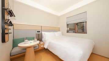 Quarto de hotel com cama, uma mesinha com chá, espelho e janela com persianas.
