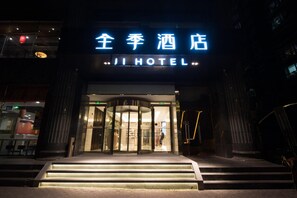 Entrada de hotel com porta de vidro, sinalização iluminada e um lance de degraus.