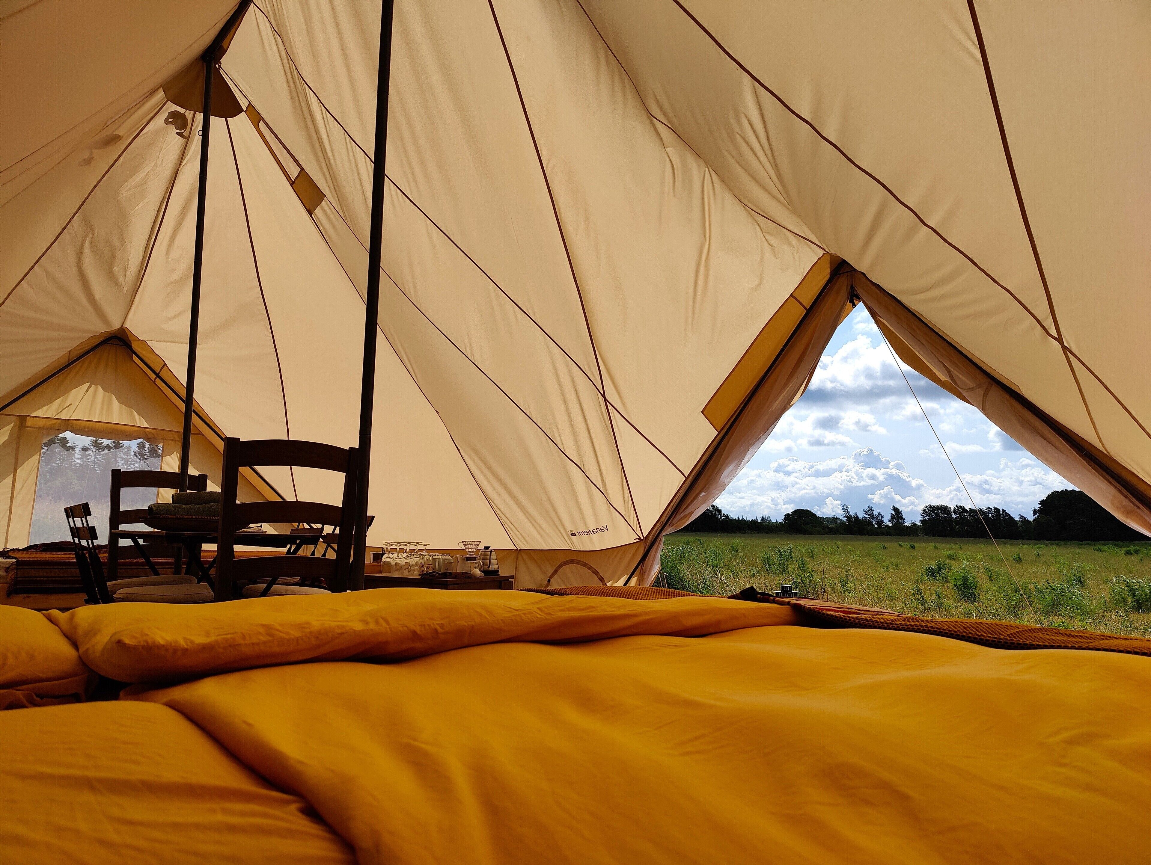 Interior de uma tenda com uma cama, cadeiras e uma mesa.
