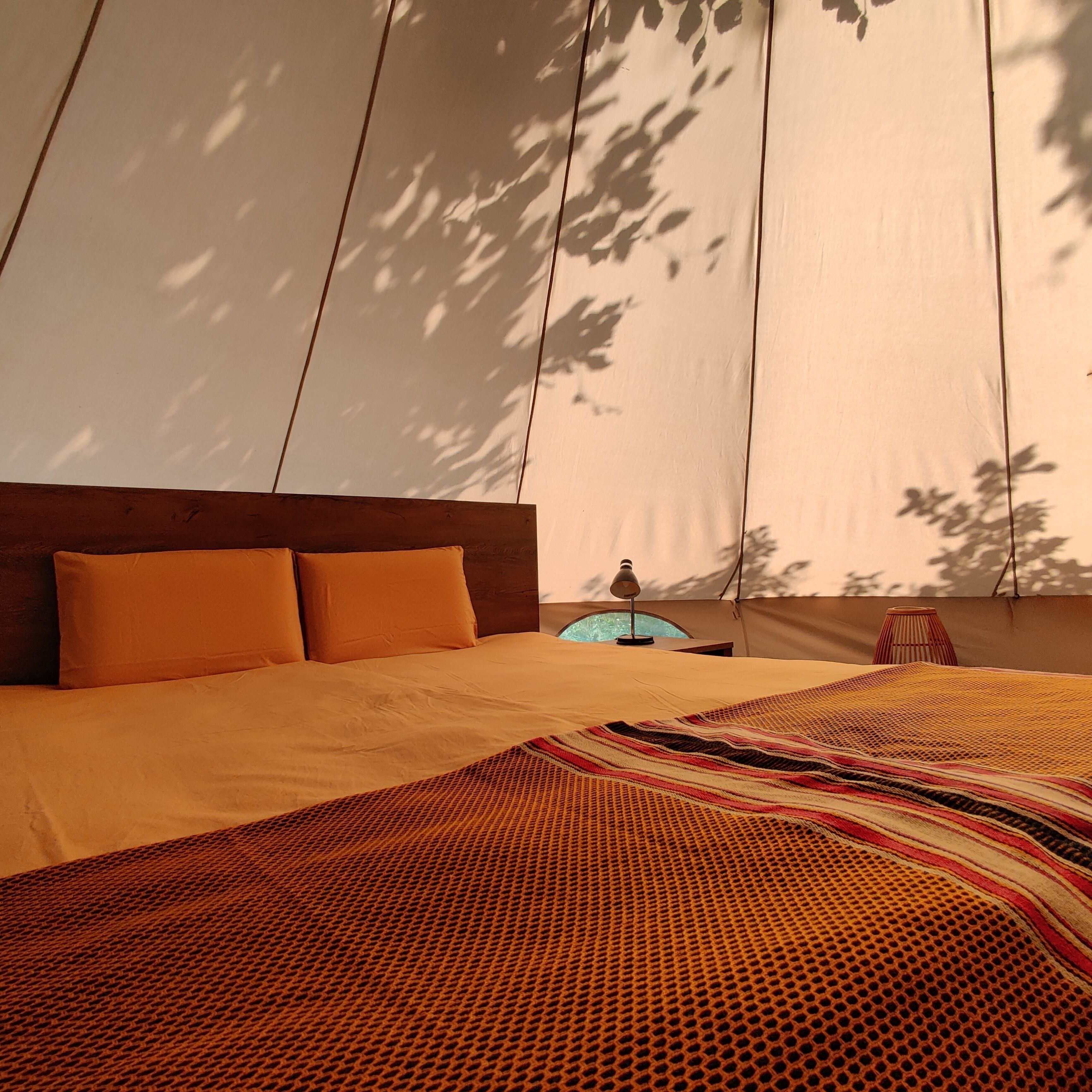 Quarto em estilo de tenda com cama, almofadas, abajur e manta de tear.