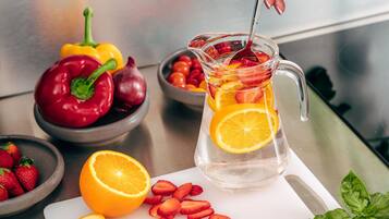 Uma bancada de cozinha com uma jarra de água saborizada com frutas, frutas frescas e uma tábua de corte.