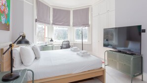Um quarto moderno com cama, escrivaninha, cadeira, televisão e janela com cortinas.