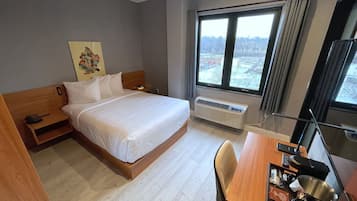 Quarto de hotel com cama, secretária com máquina de café, janela com vista e aquecedor fixado na parede.