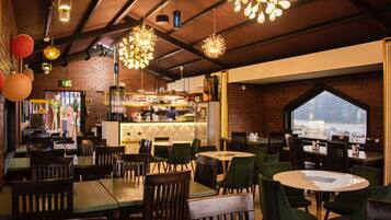 Restaurante com paredes de tijolo, cadeiras verdes e luminárias pendentes.