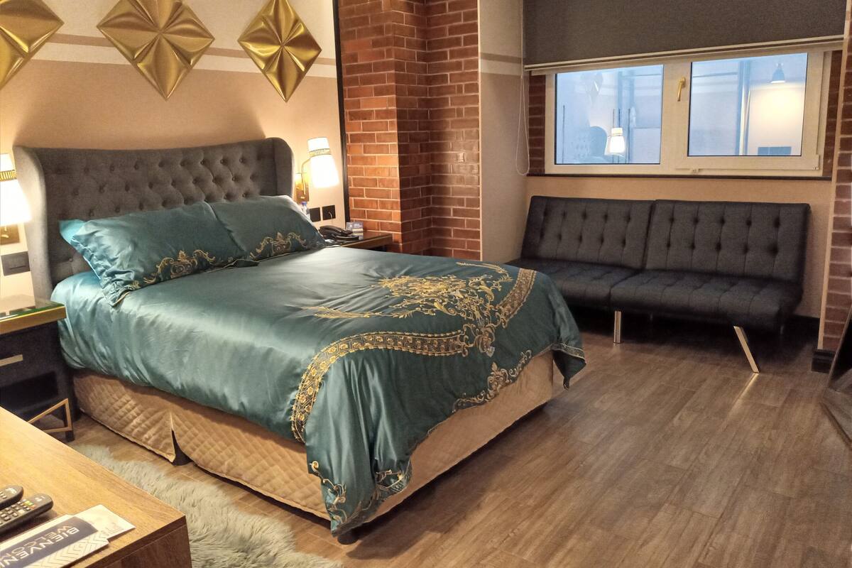 Um quarto moderno com uma cama grande, um banco, uma parede de tijolos e uma janela.