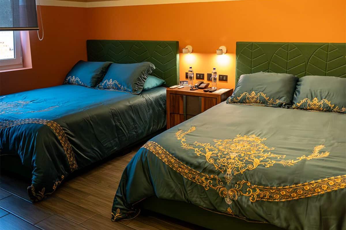 Quarto de hotel com duas camas, piso de madeira, ar-condicionado e um lustre moderno.