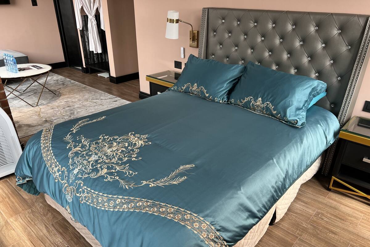 Quarto com cama grande, mesa de cabeceira, luminária na parede e pequena mesa redonda com uma cadeira.