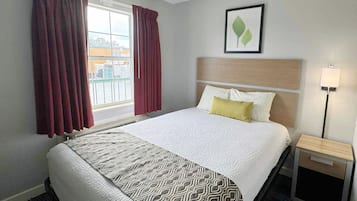 Quarto de hotel com uma cama grande, cabeceira, mesa de cabeceira com abajur e janela com cortinas.