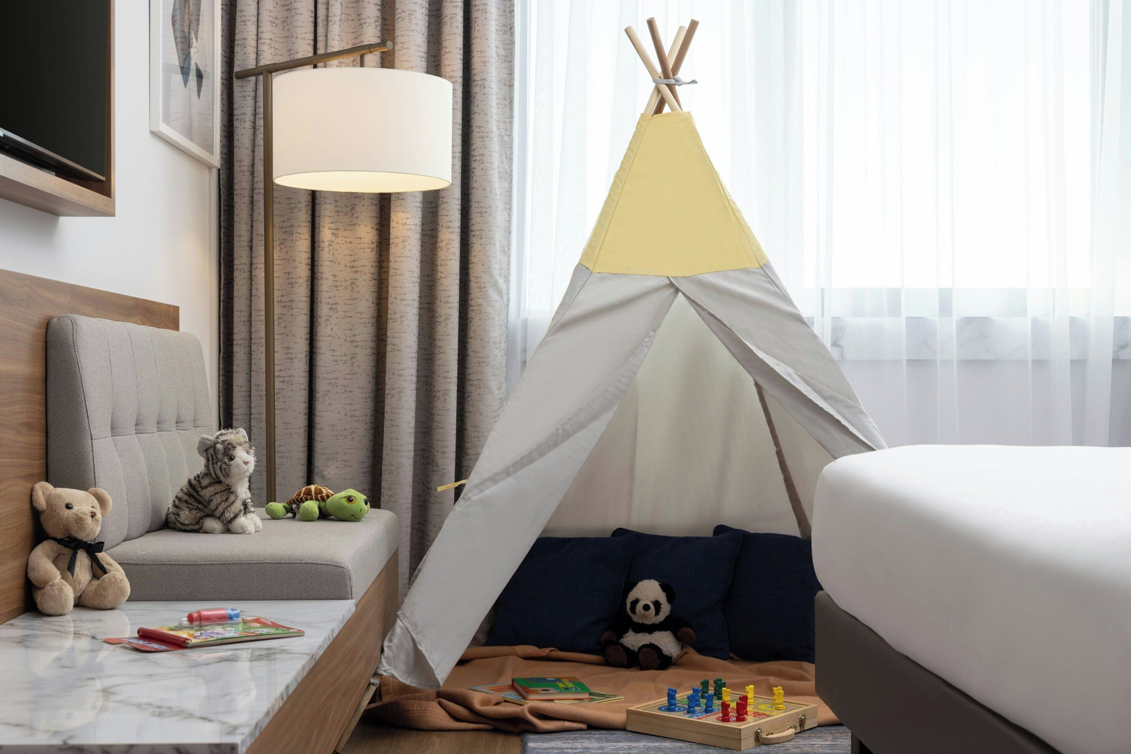 Espaço infantil com um tipi, brinquedos de pelúcia e um conjunto de brinquedos de madeira.