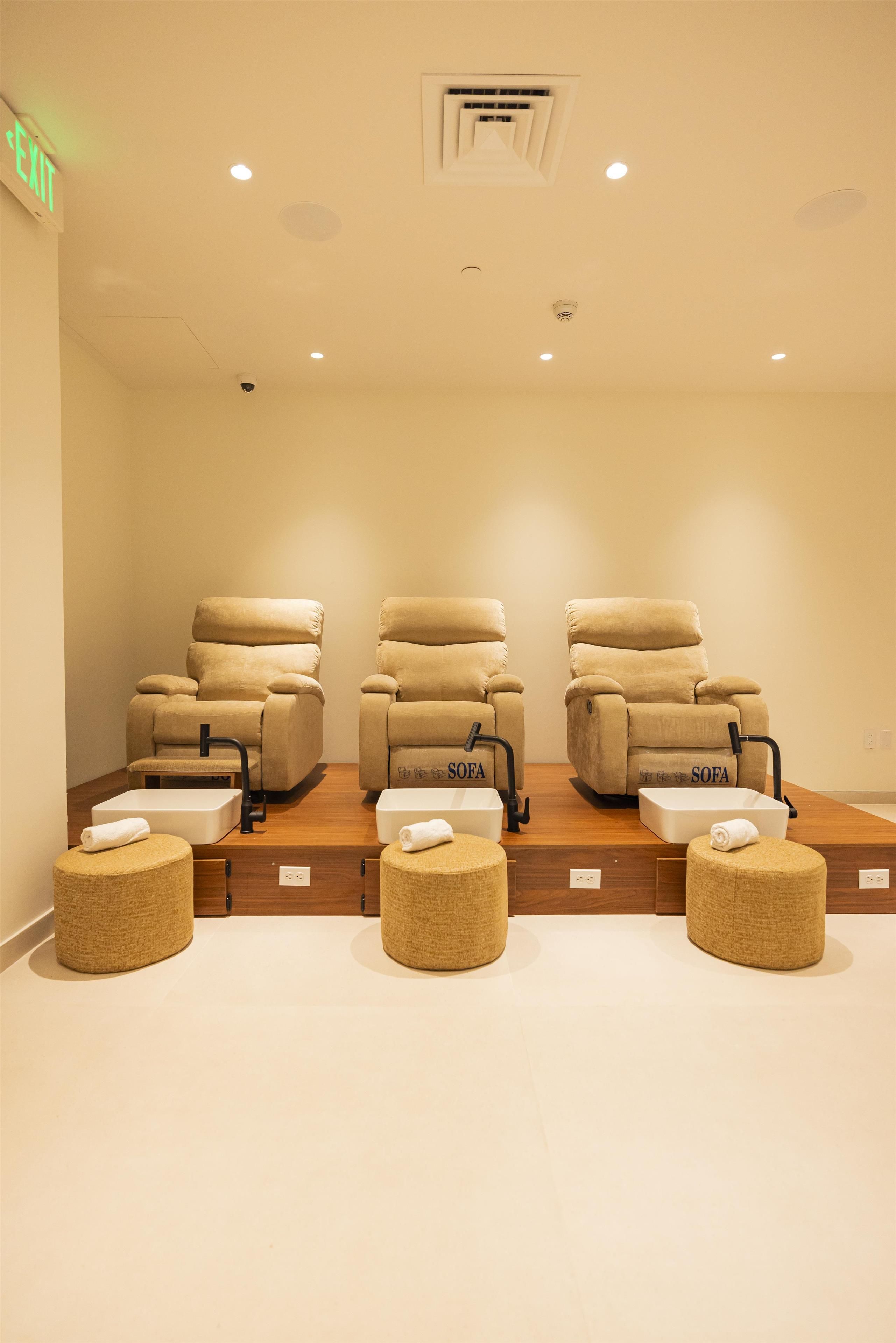 Sala de spa com três cadeiras de massagem, cada uma com apoio para os pés e uma pequena pia.